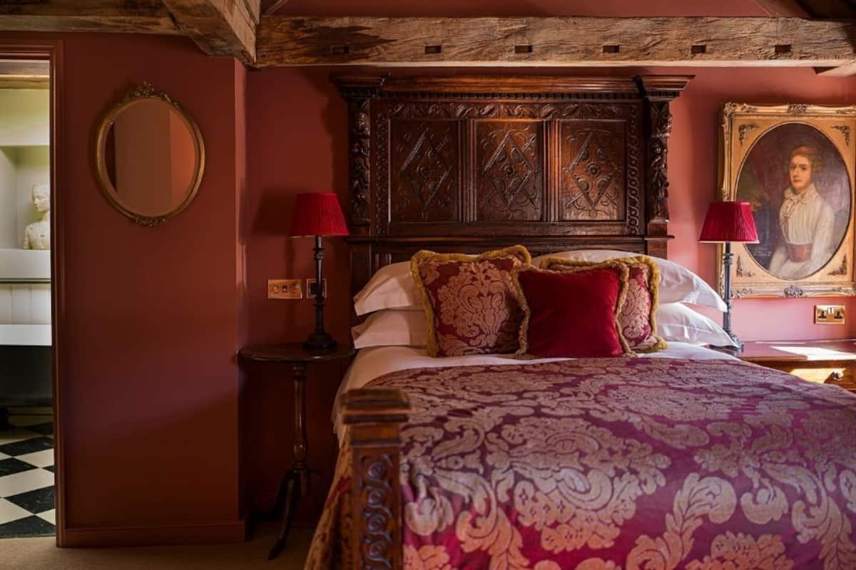 Quarto com cama grande, cabeceira decorada, um espelho e um retrato na parede.