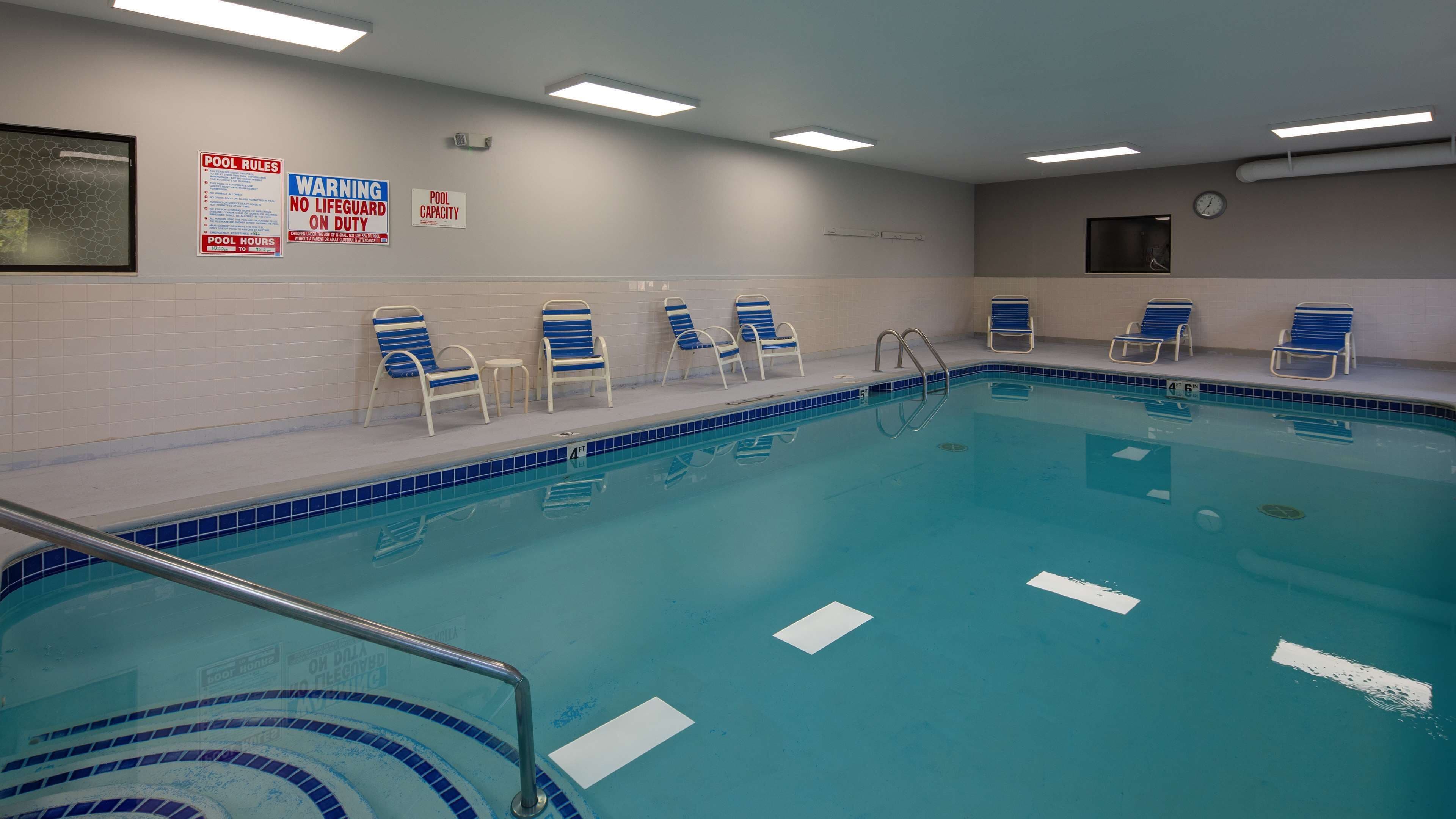Piscina interior com paredes azulejadas em azul e branco, um aviso com as 'Regras da Piscina' e várias cadeiras de descanso.
