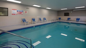 Piscina interior com paredes azulejadas em azul e branco, um aviso com as 'Regras da Piscina' e várias cadeiras de descanso.
