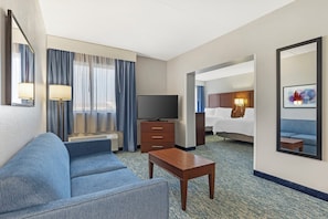 Quarto de hotel com sofá, televisão, mesa de madeira e cama com cabeceira.