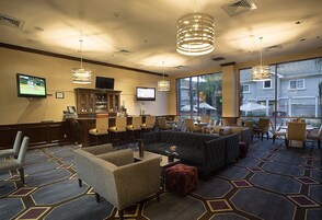 Um hall de hotel com área de bar, disposição de assentos e grandes janelas com vista para o exterior.