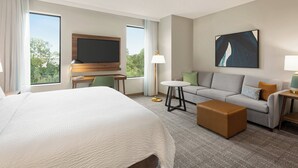 Quarto de hotel com uma cama grande, um sofá, uma mesa de centro, uma televisão e um quadro na parede.