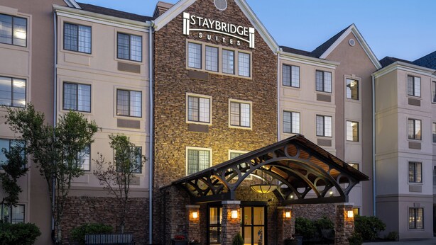 Um hotel Staybridge Suites com fachada de pedra, várias janelas e área de entrada coberta.