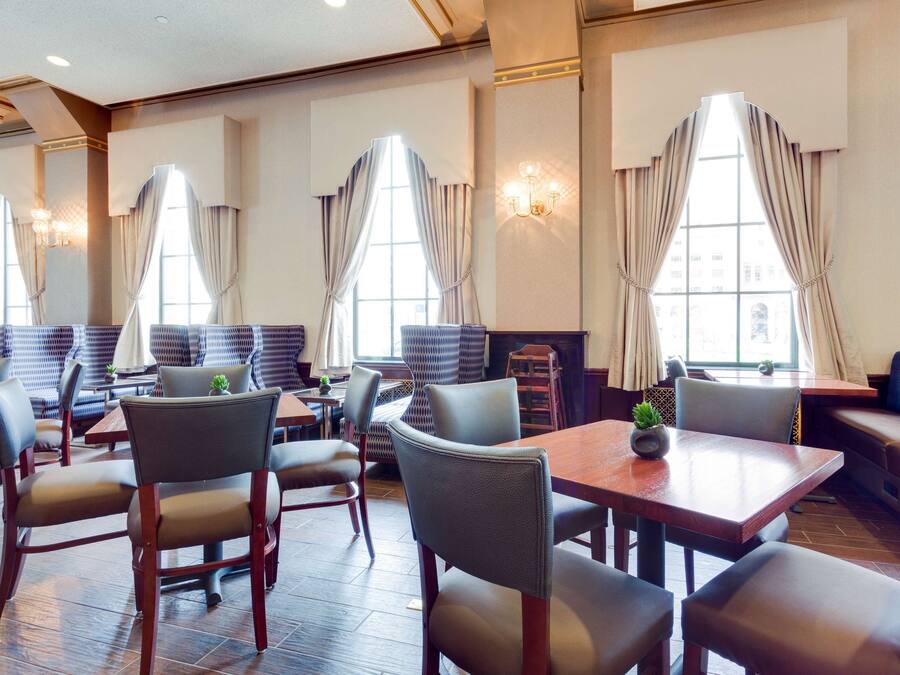 Um restaurante com cabines e mesas, janelas amplas com cortinas e um lustre.