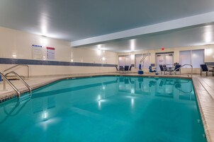 Piscina interna com água cristalina, paredes azulejadas e algumas cadeiras de descanso.