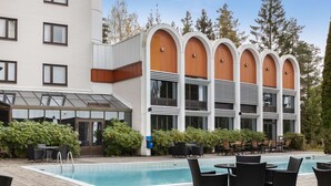 Uma área de piscina com mobiliário para área externa e um edifício com janelas em arco.