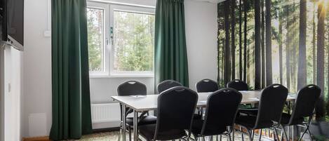 Uma sala de conferências com uma mesa, cadeiras, uma janela com cortinas e um mural com tema de floresta na parede.