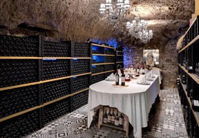 Uma adega com uma longa mesa posta para degustação, cercada por prateleiras de vinho.