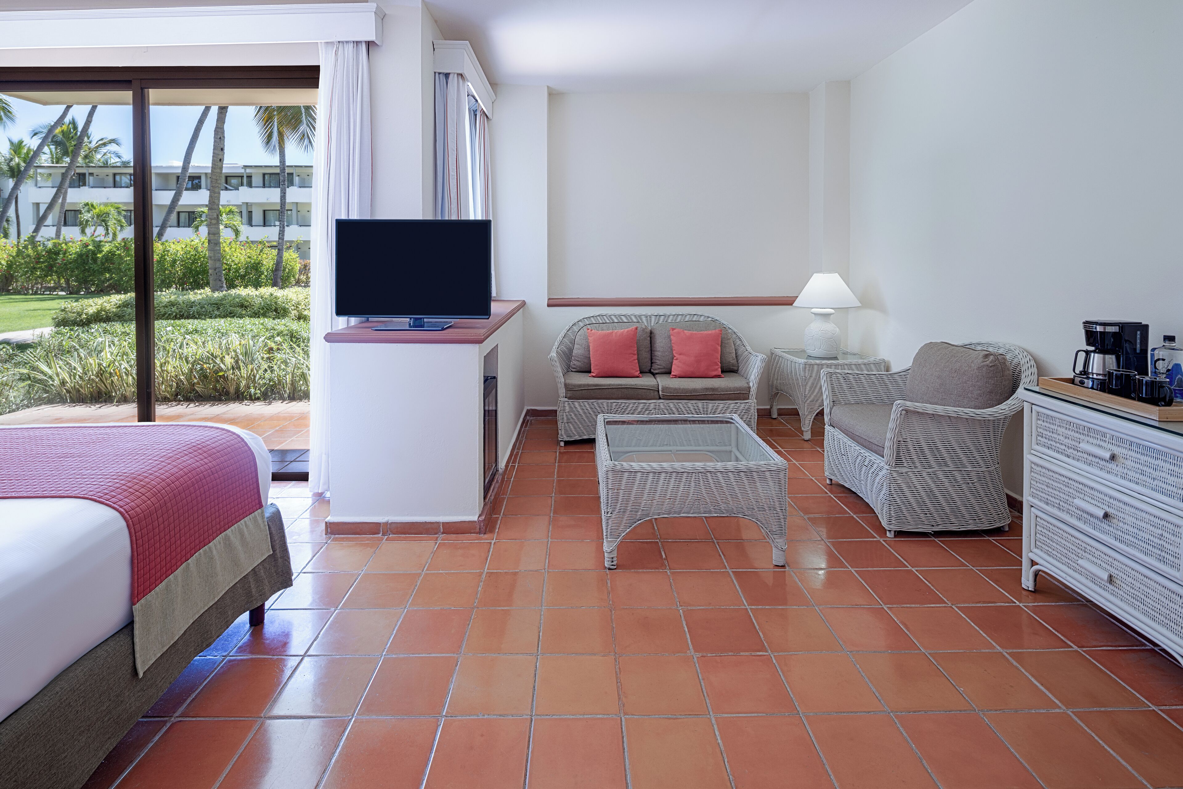 Quarto de hotel com cama, televisão, sofá, mesa de centro e área de jantar.