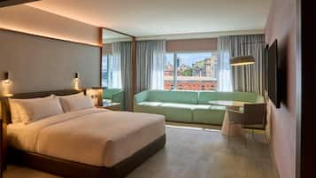 Quarto de hotel moderno com uma cama, um sofá verde, uma mesinha e uma televisão.