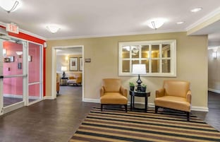Um hall com porta de saída vermelha, dois poltronas de couro, um tapete listrado e uma mesa com luminária.