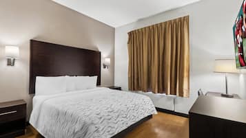 Quarto de hotel com uma cama grande, duas mesas de cabeceira, um criado-mudo, uma janela com cortinas e uma TV fixada na parede.