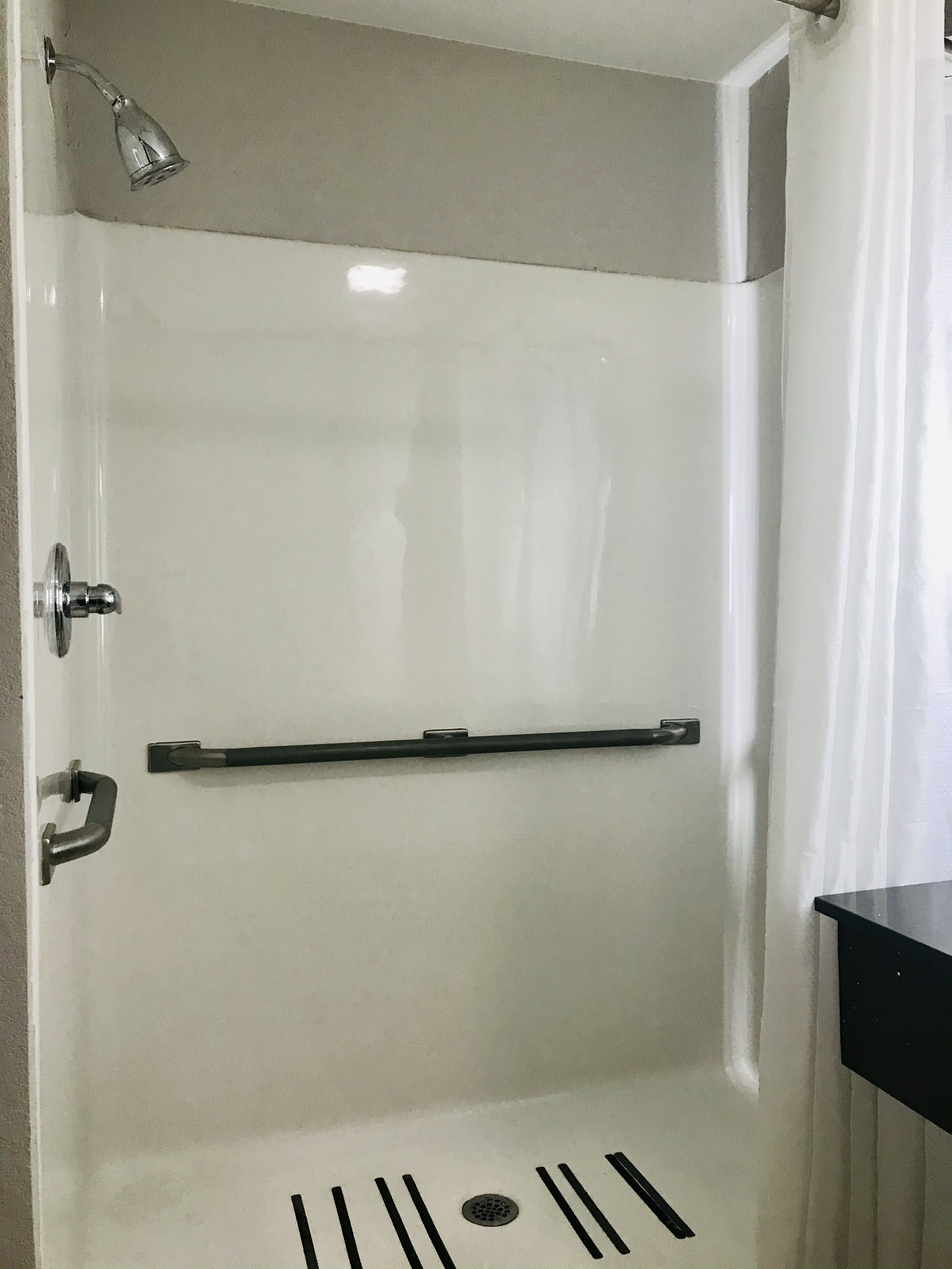 Casa de banho com chuveiro, porta-toalhas e bancada preta.