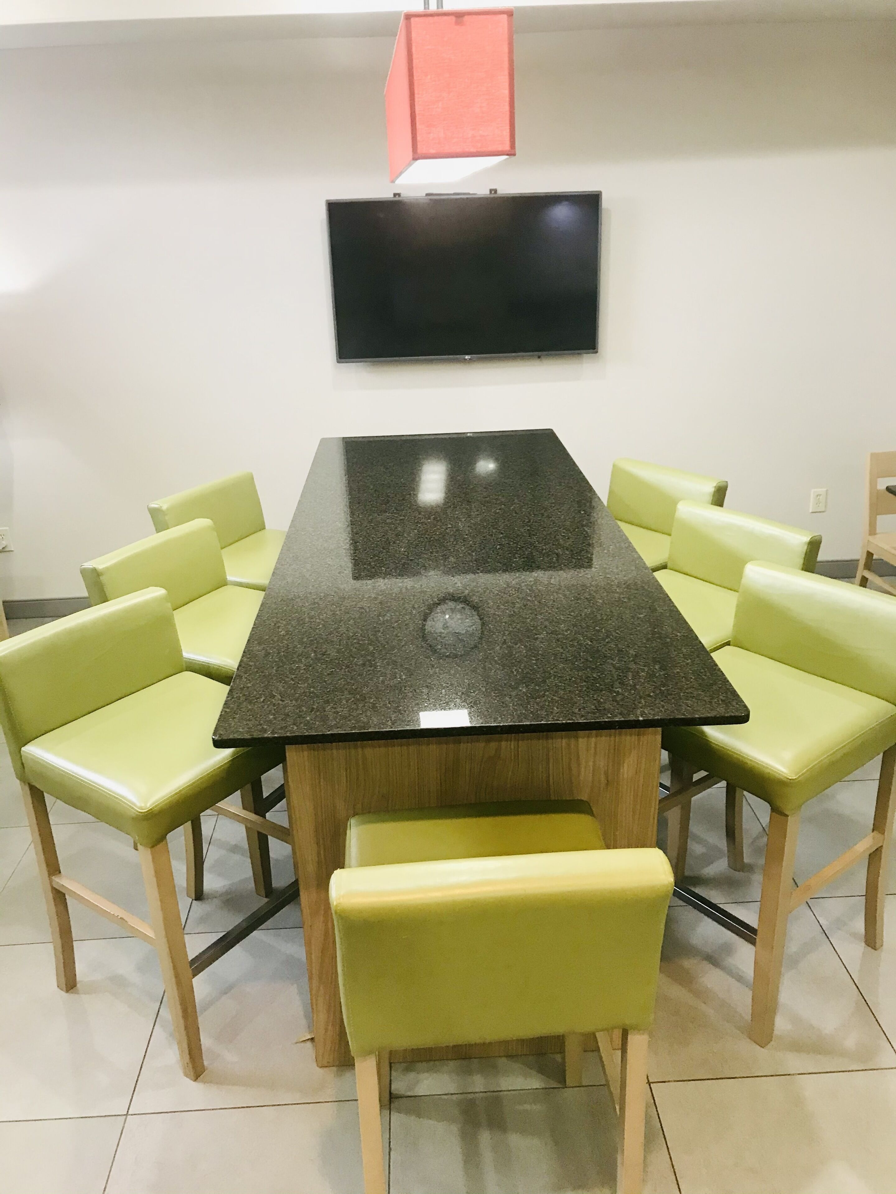 Uma sala de conferências com uma mesa retangular, seis cadeiras verdes e uma televisão de tela plana na parede.