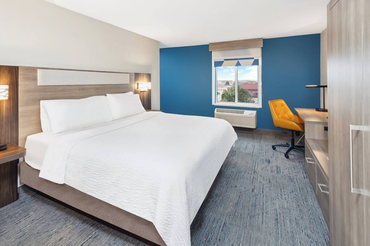 Quarto de hotel com uma cama grande, uma escrivaninha, uma cadeira e uma janela com vista.