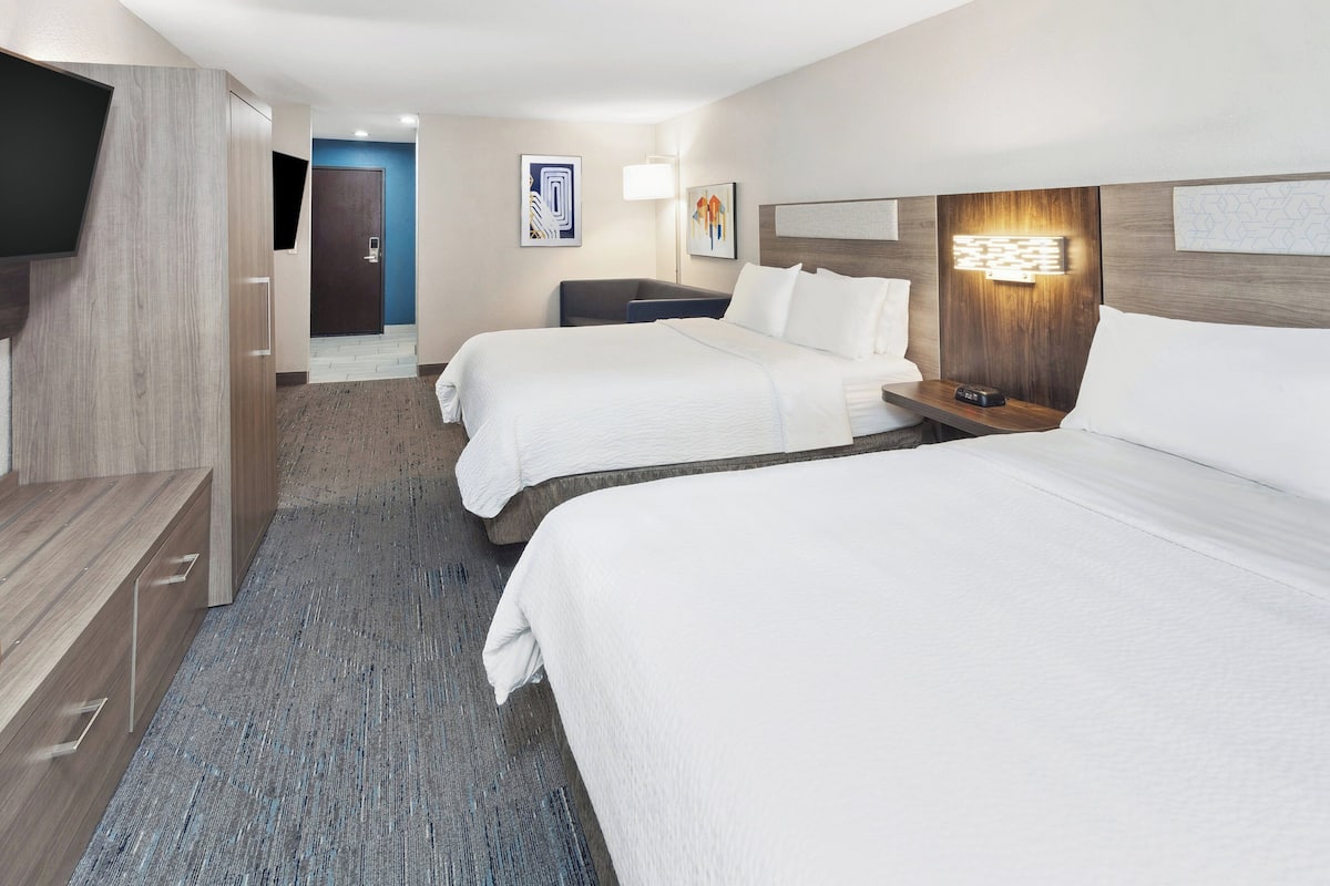 Quarto de hotel com duas camas, uma escrivaninha, televisão e porta.