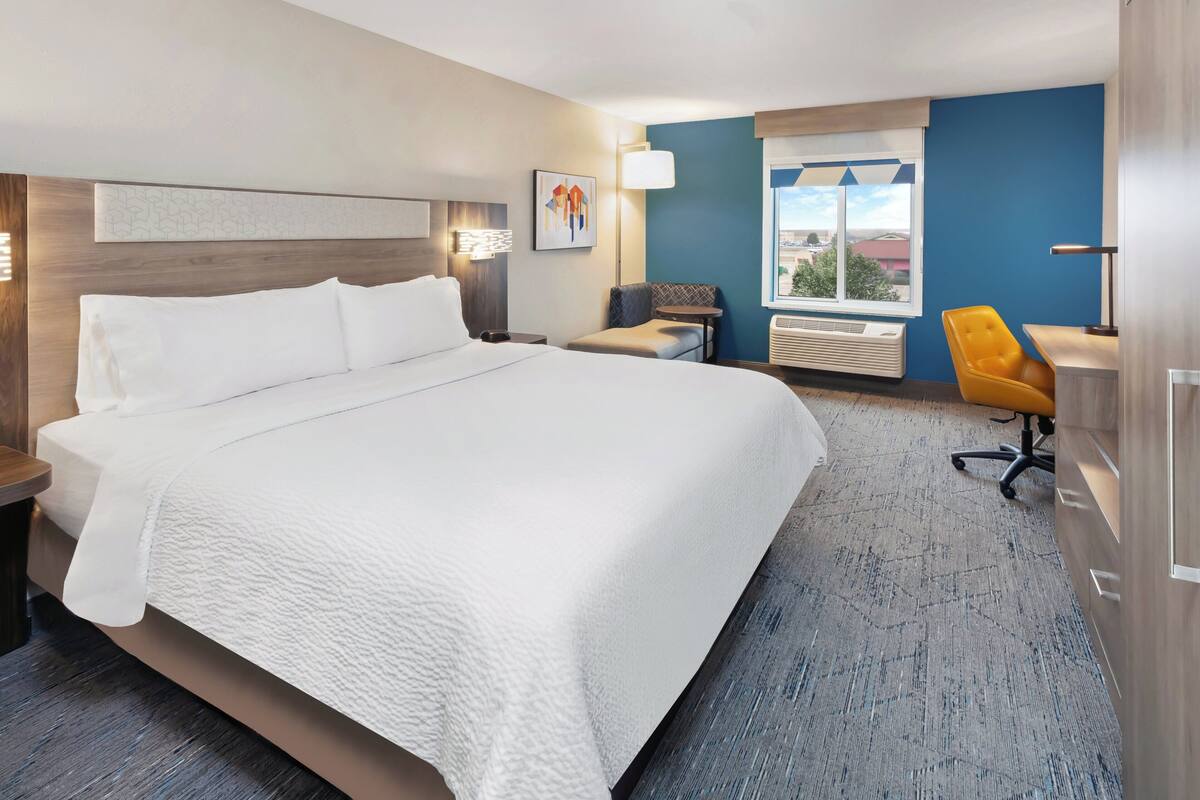 Quarto de hotel com cama grande, escrivaninha, cadeira e janela com vista.