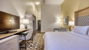 Quarto de hotel com cama, escrivaninha, cadeira, televisão e luminárias.