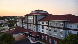Um hotel com vários andares, um logotipo verde marcante, estacionamento e uma área arborizada.