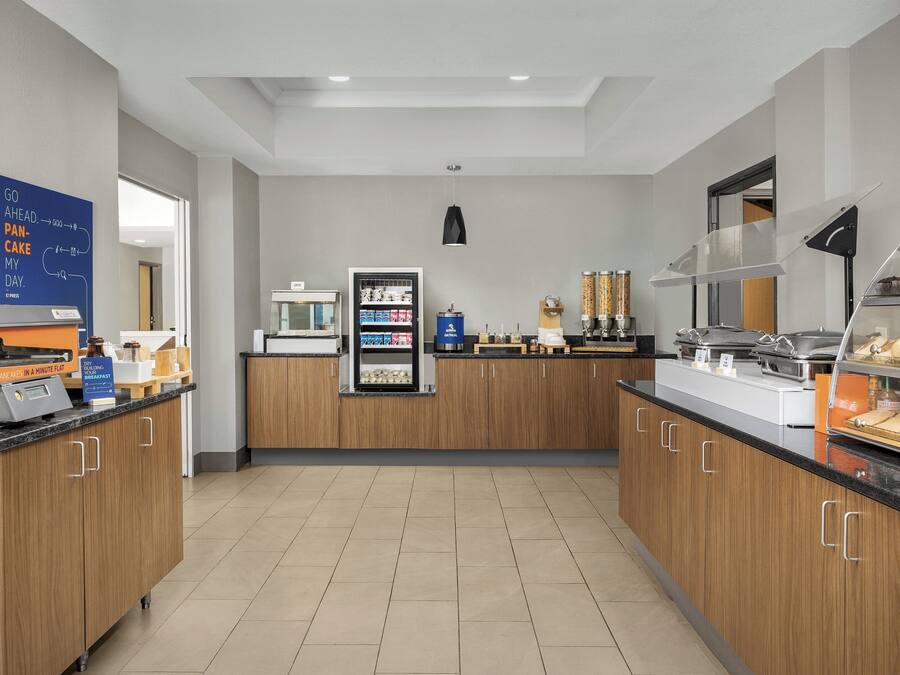Cozinha moderna com estação de café da manhã estilo buffet, incluindo máquina de café, geladeira e vitrine com doces.