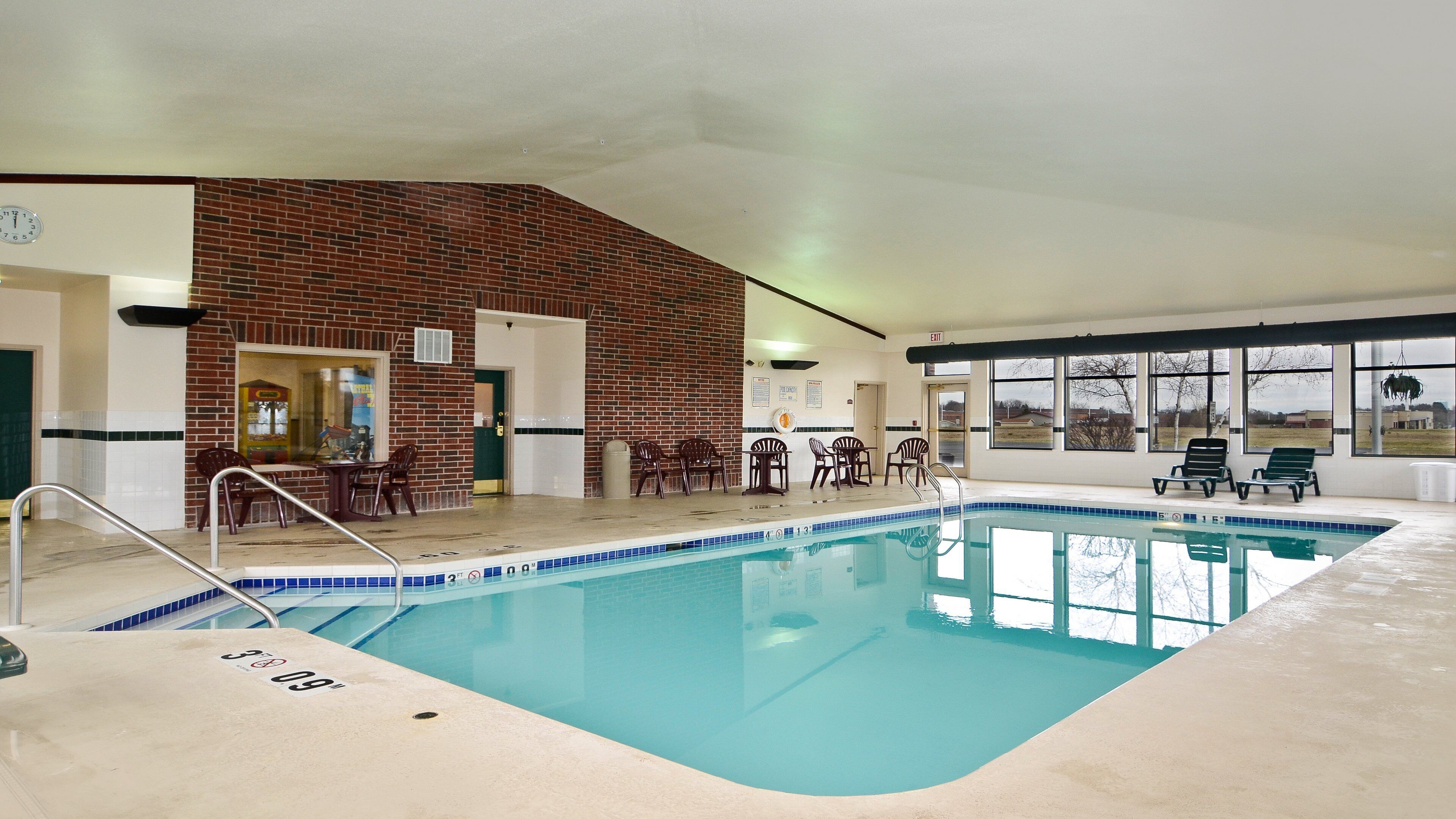 Piscina interna com parede de tijolos, área de estar e janelas.