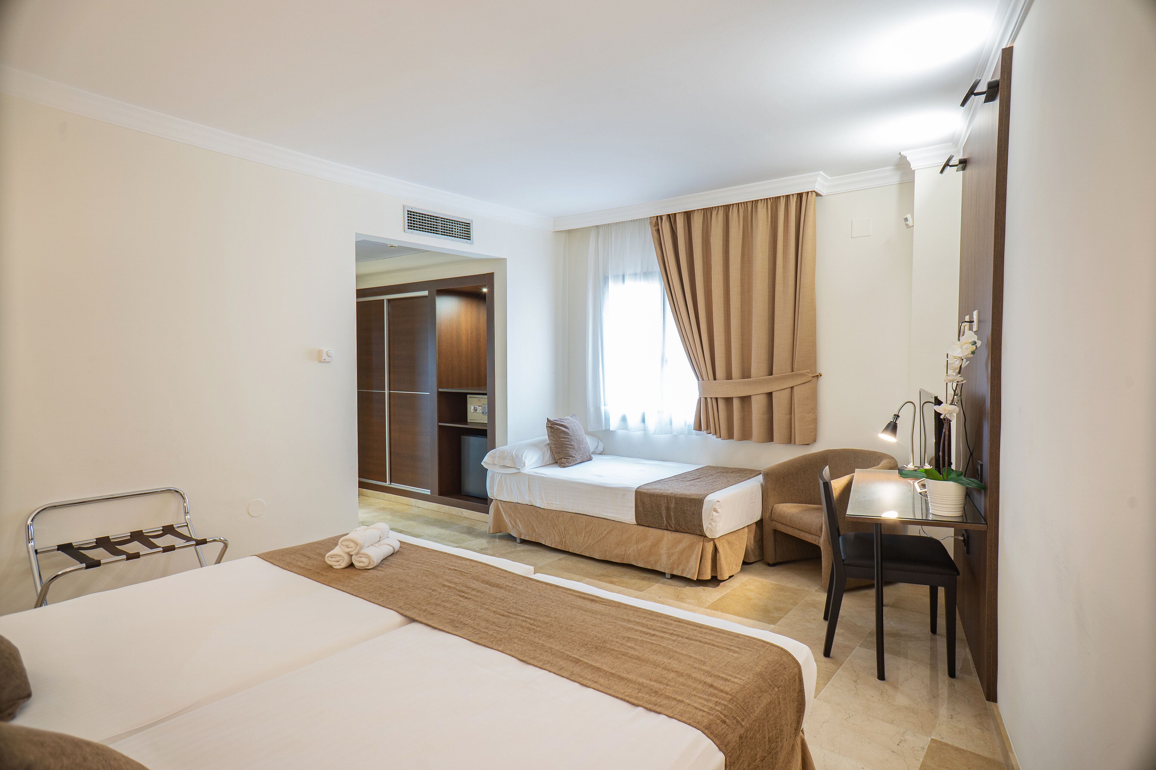 Quarto de hotel com cama, escrivaninha, cadeira e armário.