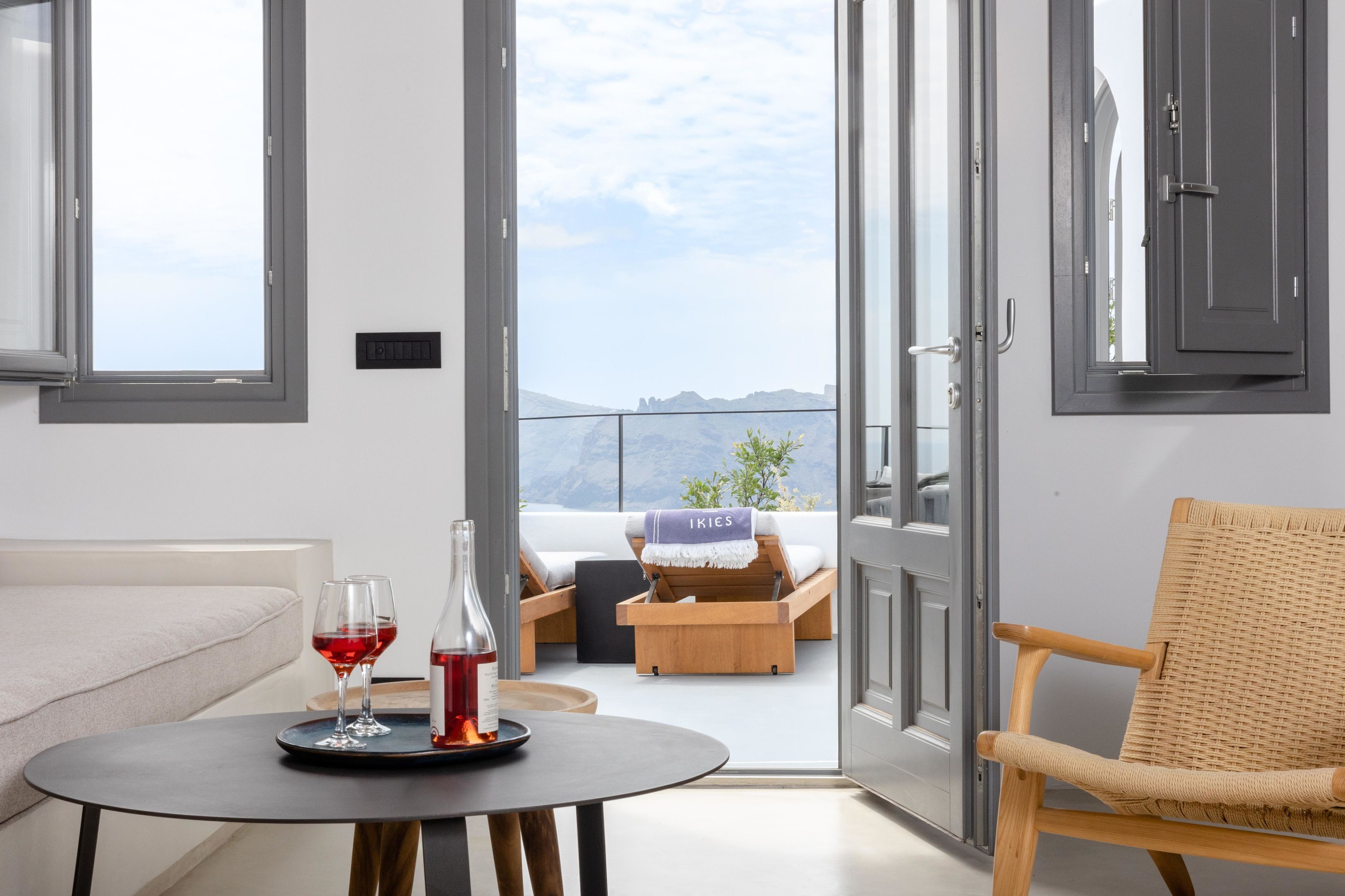 Quarto moderno com varanda, sofá, mesa com copos e uma garrafa, e cadeira de vime.