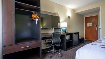 Quarto de hotel com cama, escrivaninha, computador, televisão, guarda-roupa e abajur.