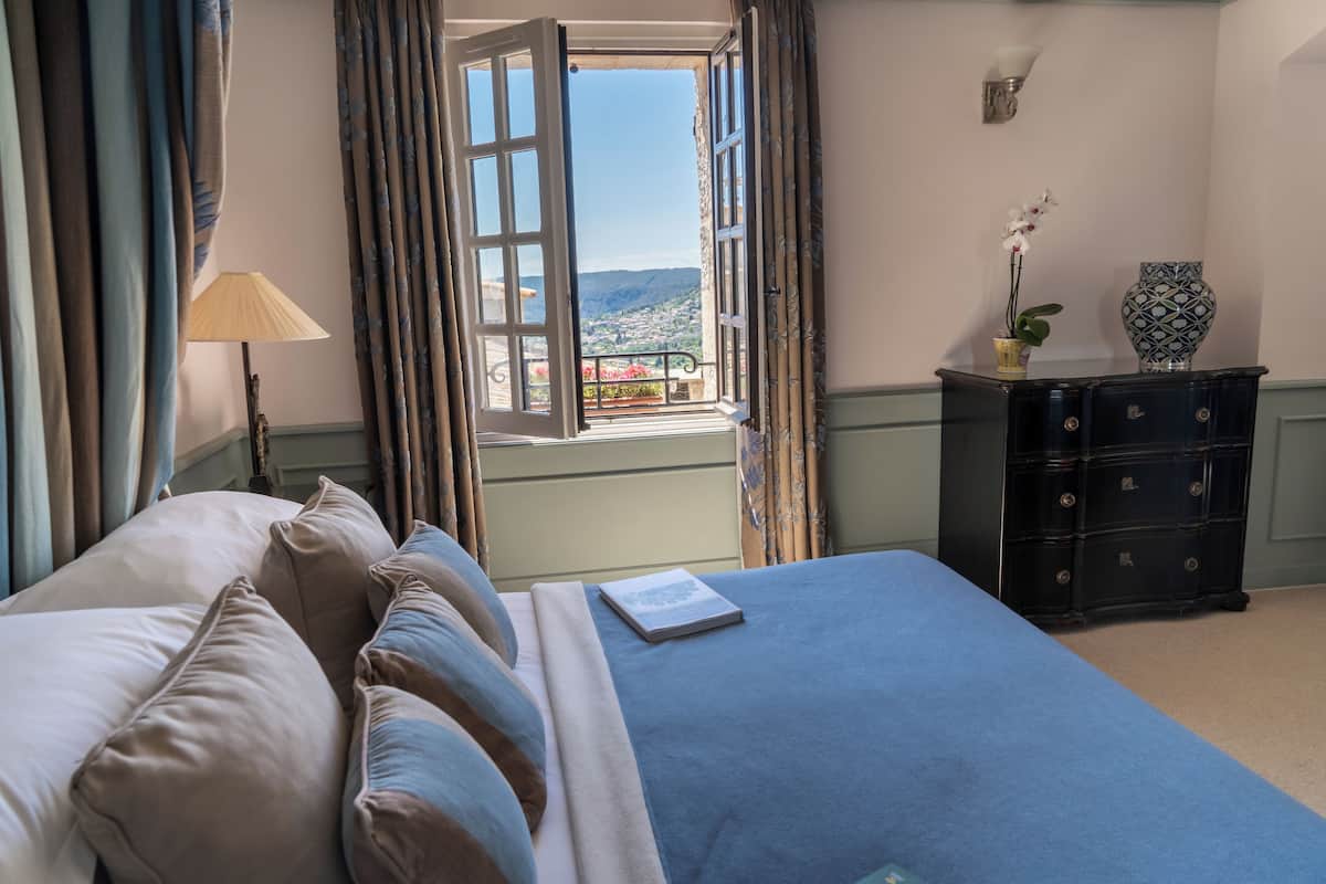 Quarto com cama grande, janela com cortinas, cômoda e vaso com flores.