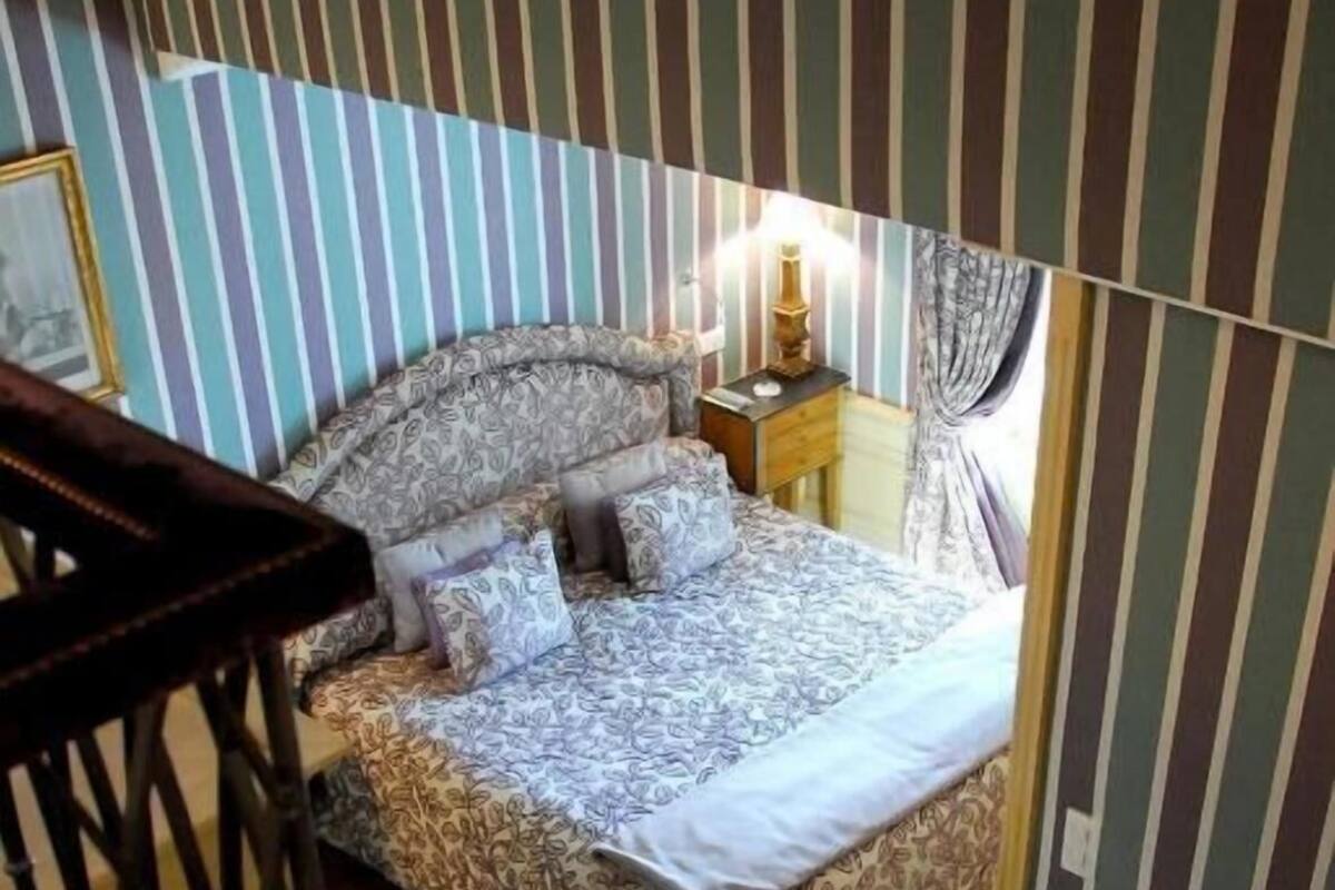Quarto com colcha estampada, mesa de cabeceira com abajur e parede listrada.