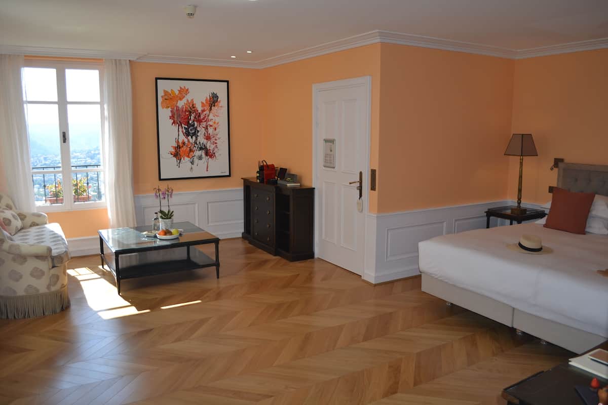 Quarto com sofá branco, mesa de centro de vidro, armário de madeira escura e cama com cabeceira branca.