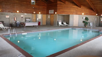 Piscina interna com teto de madeira, mesa de bilhar e cadeiras de descanso.