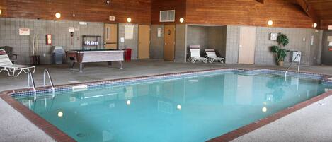 Piscina interna com teto de madeira, mesa de bilhar e cadeiras de descanso.