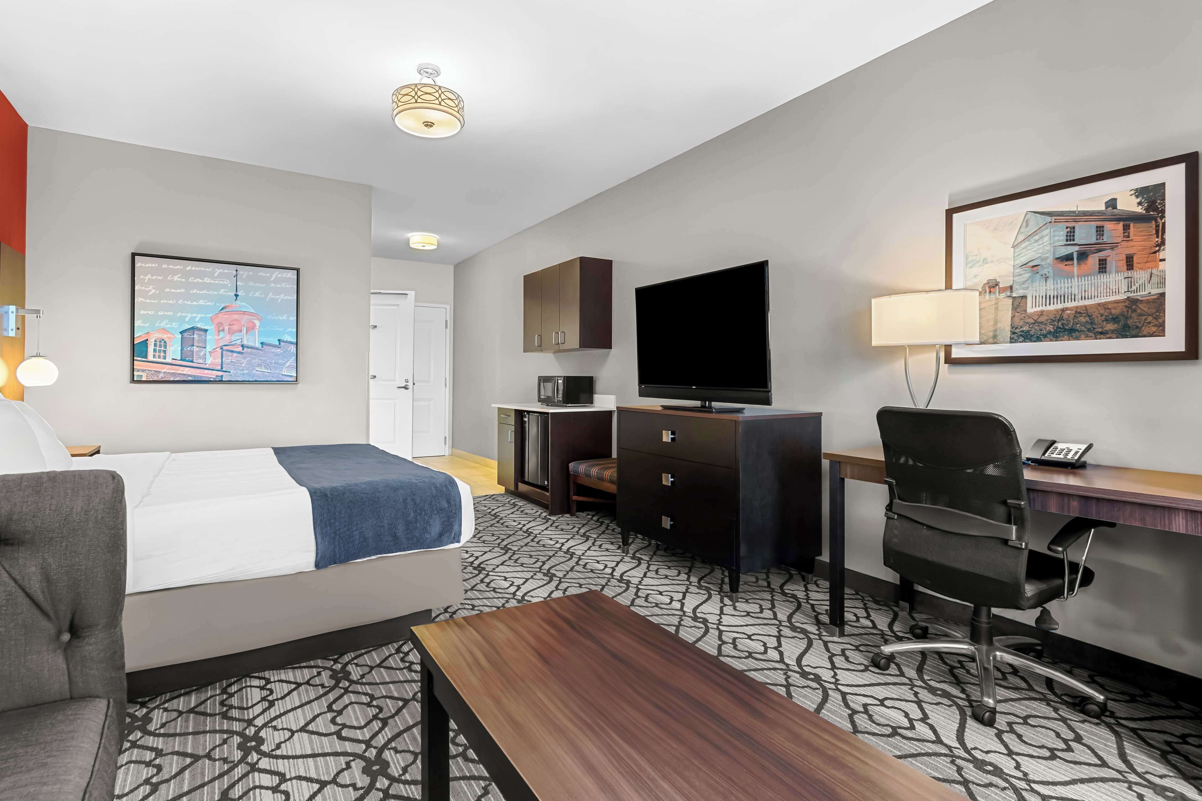Quarto de hotel com cama, escrivaninha, cadeira, televisão e obras de arte nas paredes.