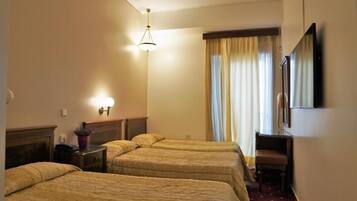 Quarto de hotel com três camas, uma escrivaninha, uma cadeira e uma televisão.