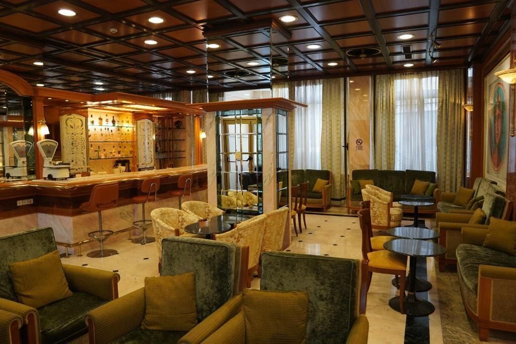 Um hall de hotel com área de bar, disposição de assentos e uma grande janela.