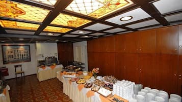 Uma sala de banquetes com uma mesa comprida preparada para um buffet, painéis de madeira nas paredes e teto com janelas de vitrais.