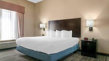 Quarto de hotel com uma cama grande, duas mesas de cabeceira, um criado-mudo, uma luminária na parede e uma janela com cortinas.