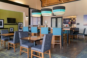 Restaurante moderno com cadeiras estofadas em azul, mesas de madeira e iluminação pendente.