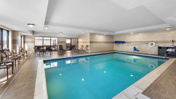 Piscina interior com água azul cristalina, cercada por espreguiçadeiras e um espaço de estar com mesas.