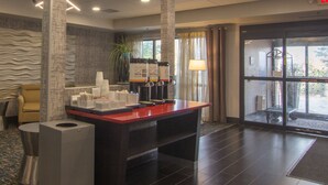 Um hall de hotel com balcão de recepção, área de café, espaço para sentar e uma grande janela.