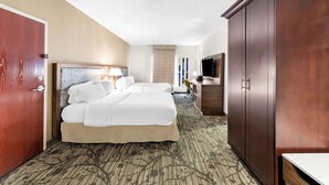 Quarto de hotel com cama grande, guarda-roupa, secretária e televisão.