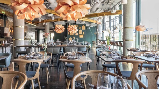 Restaurante com mesas redondas, cadeiras e decorações laranja penduradas.