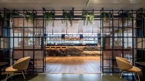 Uma área de bar moderna com piso de madeira, dois espaços de estar com cadeiras e um balcão de bar com prateleiras de garrafas.