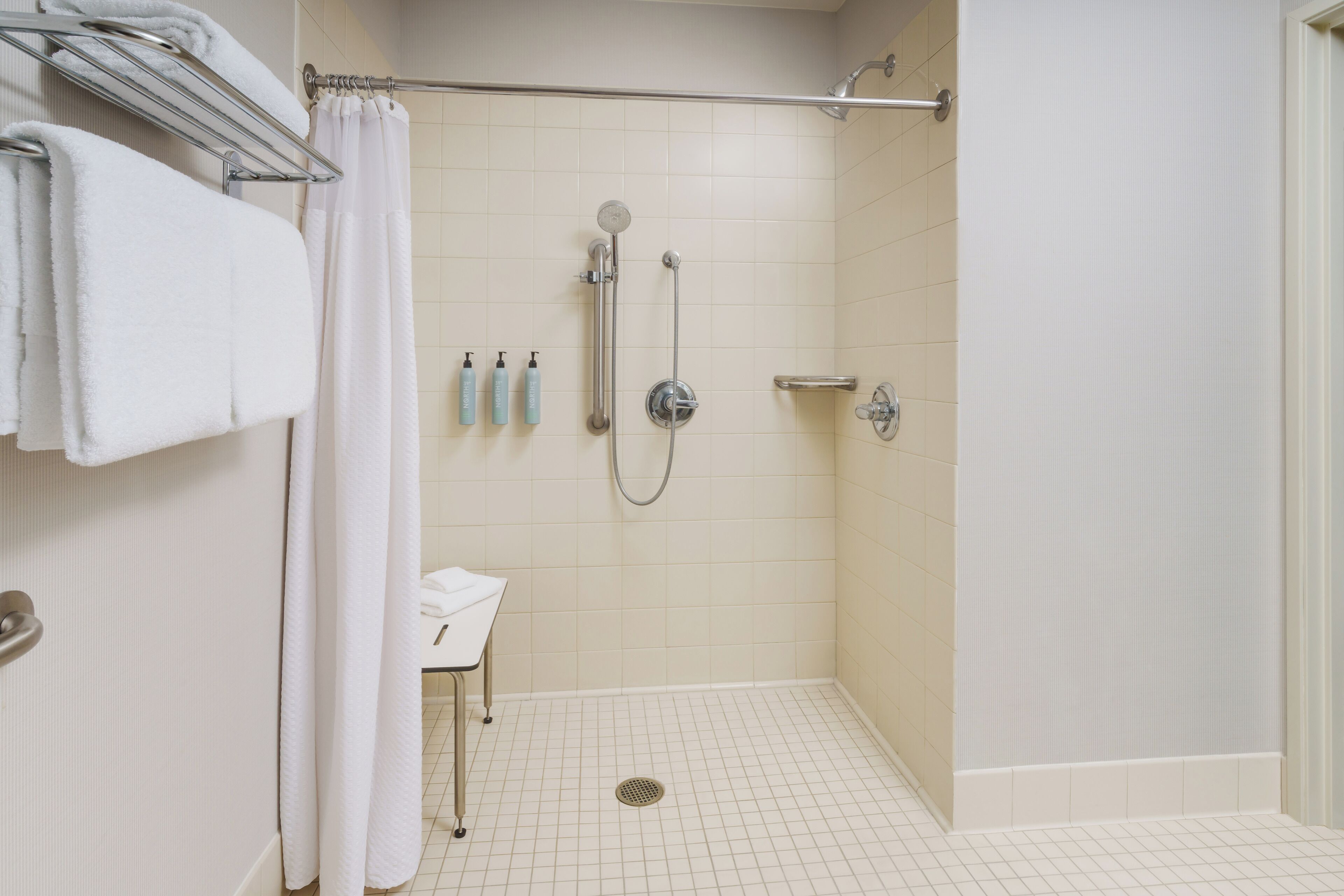Um pequeno espaço com chuveiro revestido em azulejos, com chuveiro fixo e de mão, além de um porta-toalhas.