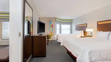 Quarto de hotel com duas camas, uma mesa de trabalho, televisão, uma cadeira, janela e luminária.