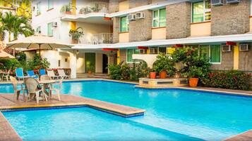 Um hotel com piscina, área de estar externa e plantas em vasos.