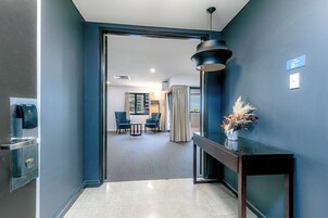 Um corredor com parede azul escura, um console de madeira com um vaso e uma porta que dá para um espaço com área de jantar.