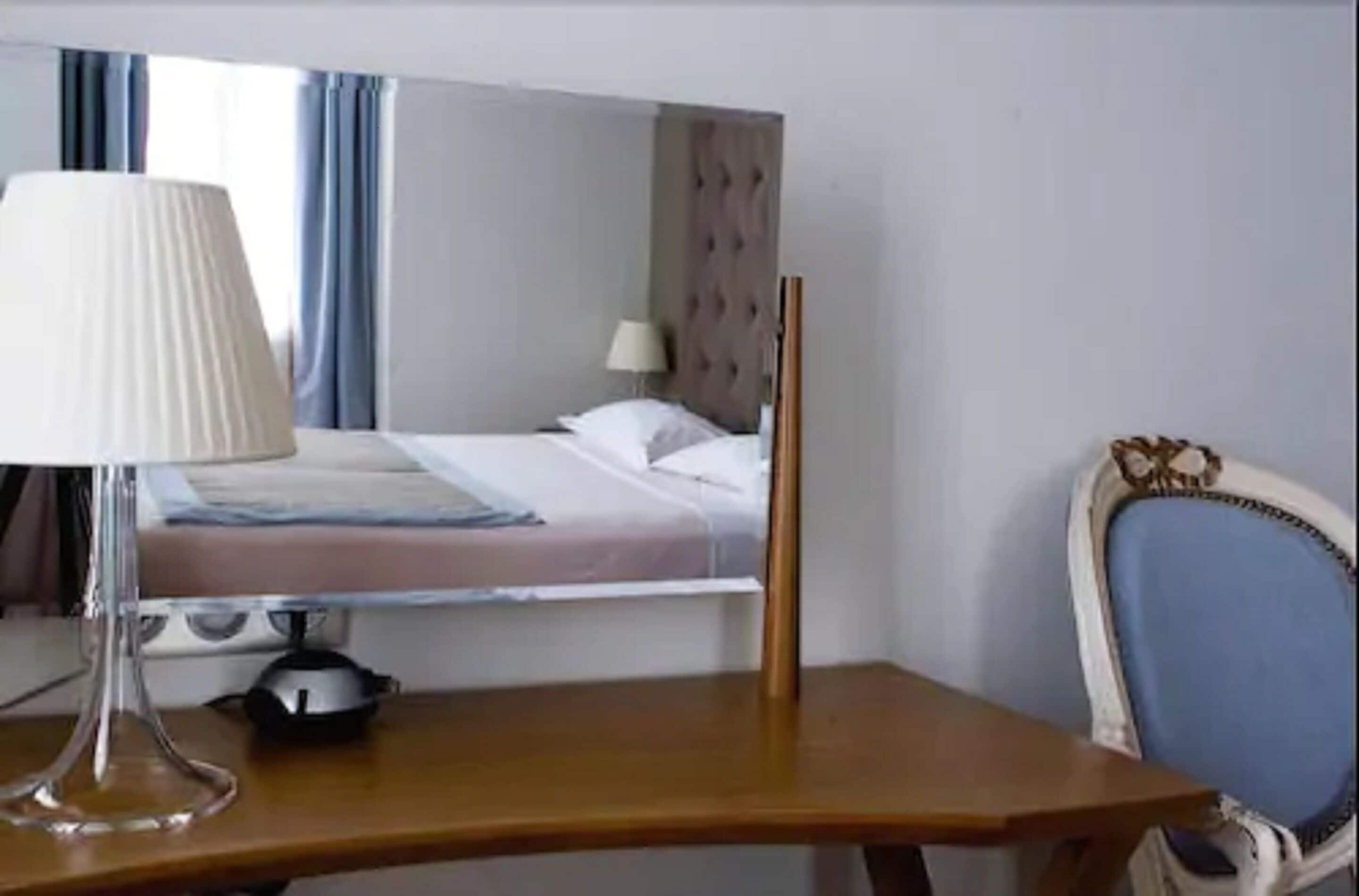 Quarto de hotel com cama, mesa de cabeceira com abajur, uma cadeira e janela com cortinas.