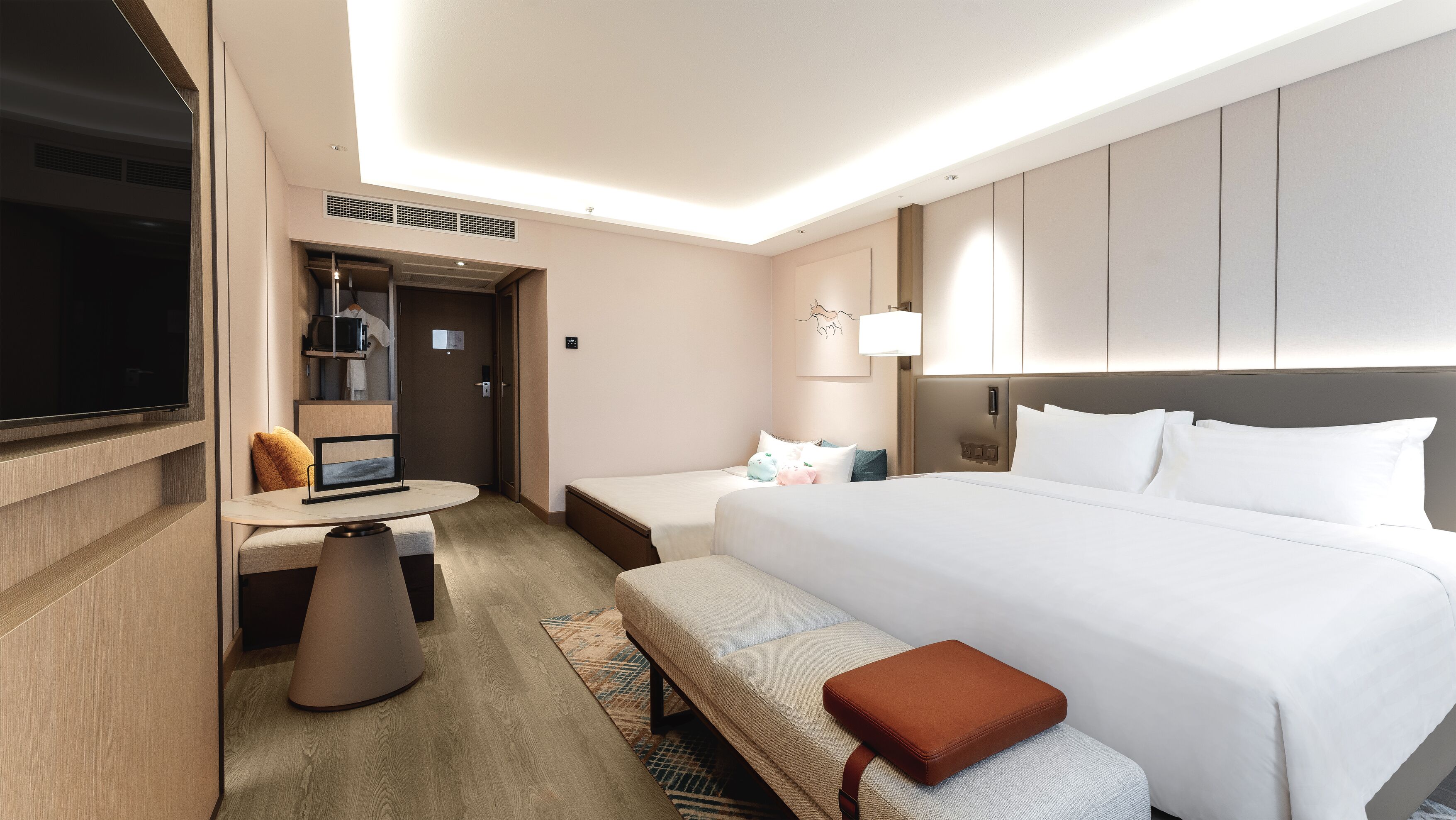 Quarto de hotel com cama grande, escrivaninha com televisão de tela plana, área de estar com poltrona e apoio para os pés, e porta que dá para um armário.